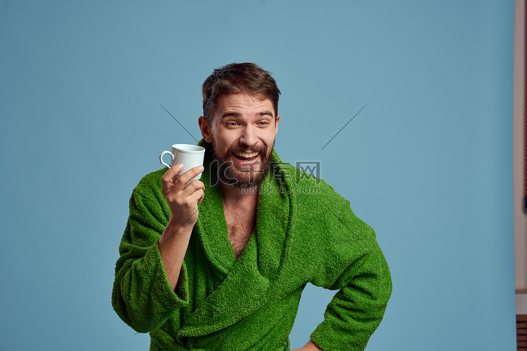 穿着温暖长袍的冰冻男人，在蓝色背景的裁剪视图上喝着一杯热饮高清摄影大图-千库网