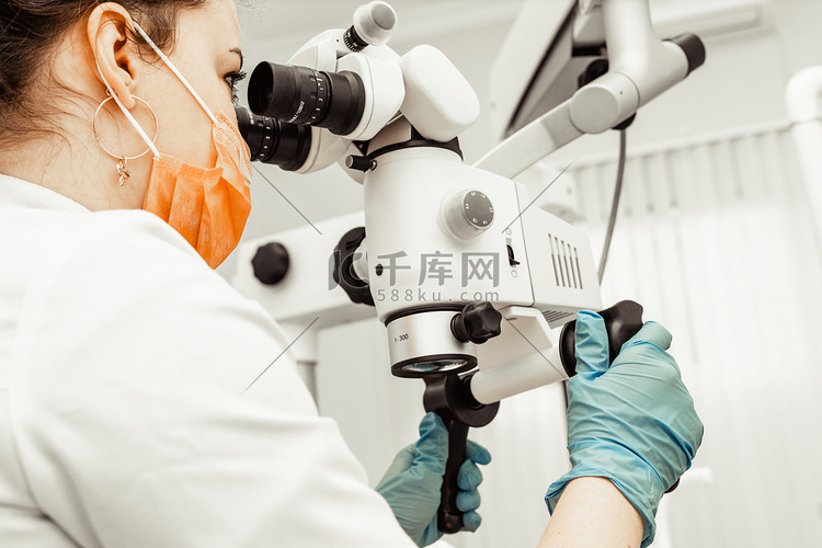 年轻的女牙医通过牙科诊所的专业显微镜进行观察。高清摄影大图-千库网