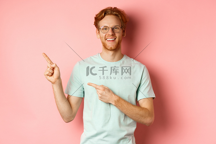 开朗的红发年轻人的肖像,戴着眼镜,手指指向左上角,微笑着,站在粉红色的背景上高清摄影大图 千库网
