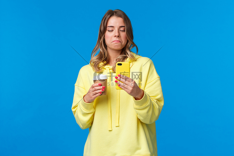 女孩在智能手机屏幕上查看自己的照片，表情不错，在移动应用程序中编辑图片后，看起来很高兴，但并不赞同，用纸杯喝咖啡高清摄影大图-千库网