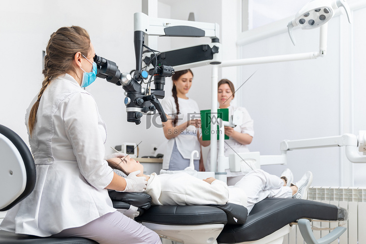 女性牙医在牙科诊所办公室使用牙科显微镜治疗患者牙齿高清摄影大图-千库网