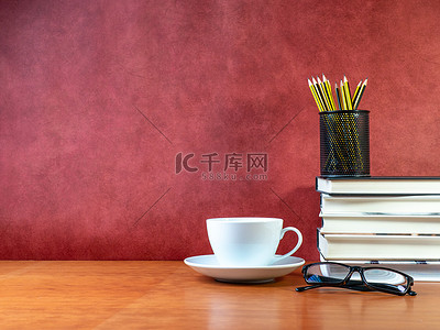 木桌和红色 backg 上的杯子、书籍、眼镜和铅笔罐高清摄影大图-千库网