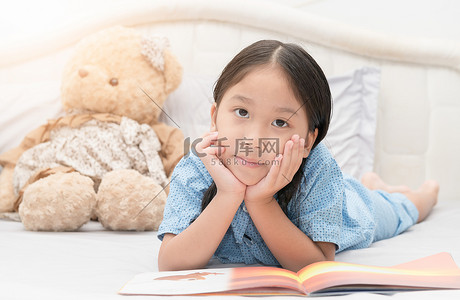 可爱的小亚洲女孩读童话书在床上高清摄影大图-千库网