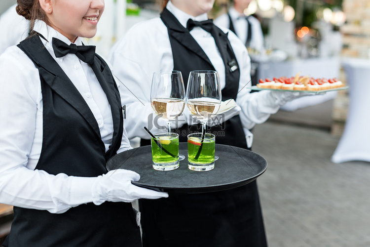在自助餐宴会、节庆活动或婚礼期间，有一半的职业服务员身穿制服，为客人提供葡萄酒、鸡尾酒和零食。满满一杯酒放在盘子里.户外派对饮食服务高清摄影大 ...