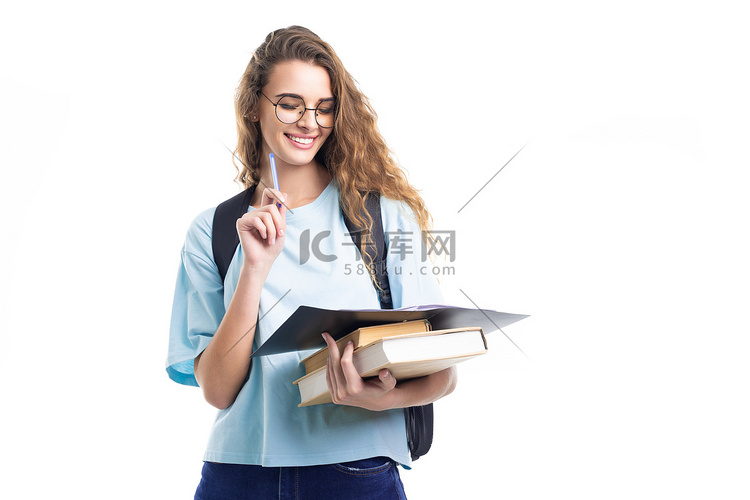 Smiling student girl holds pencil and books while looking at notebook ...
