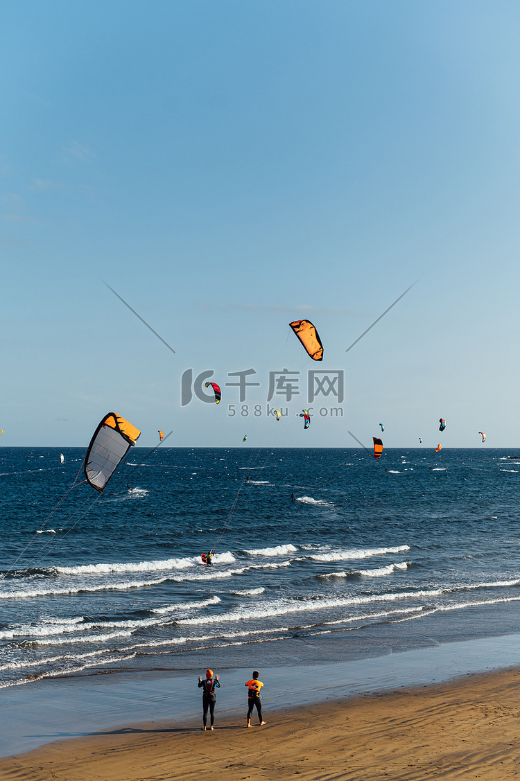 Many colorful kites on beach and kite surfers riding waves during windy ...