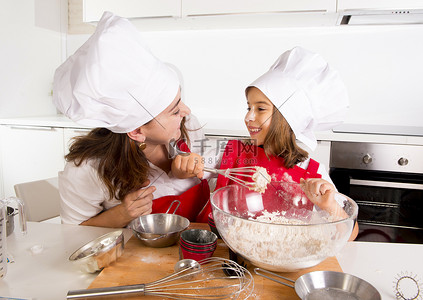happy mother baking with little daughter in apron and cook hat with ...