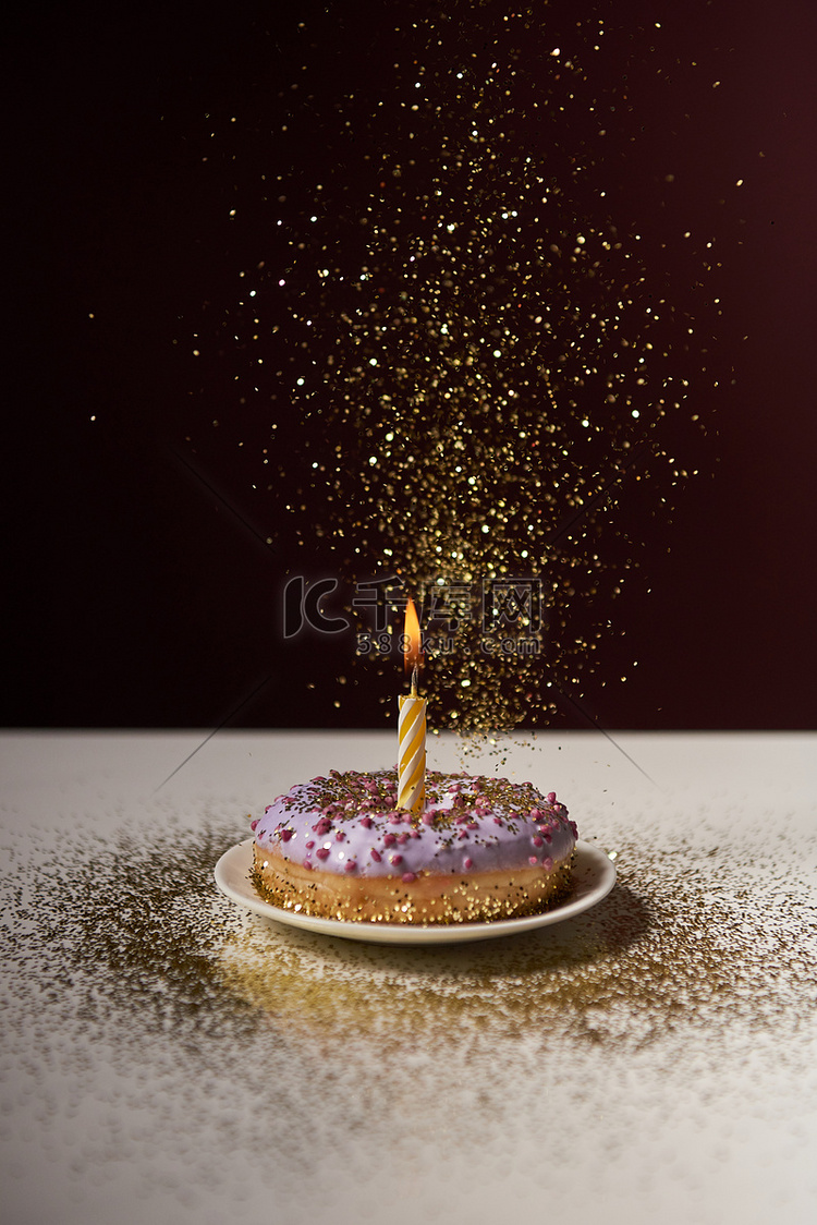 burning candle in middle of doughnut with falling sparkles on white ...