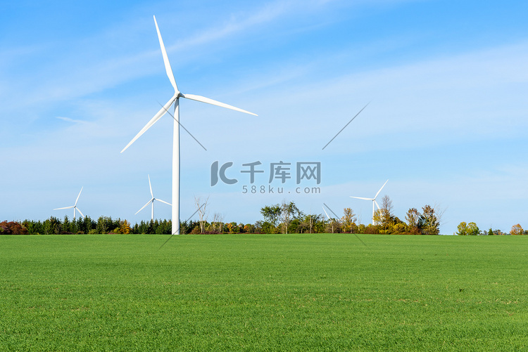 Tall wind turbine in a meadow bordered with autumn trees on a sunny ...