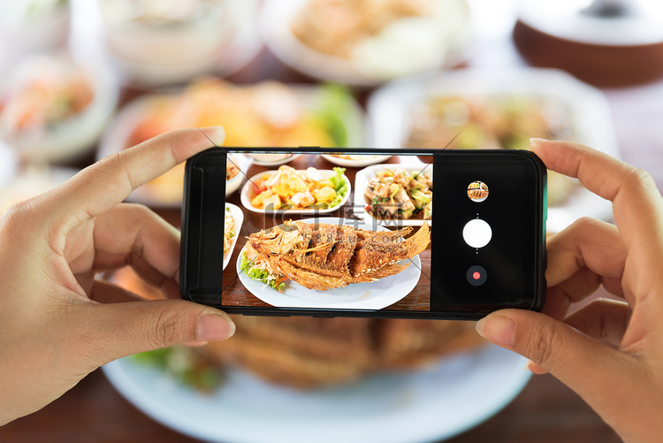 Woman taking a photo of food with smartphone in restaurant.高清摄影大图-千库网