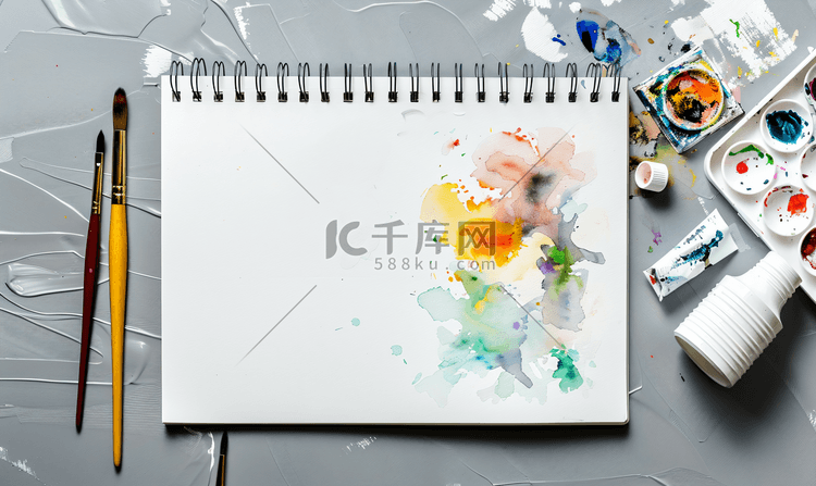 灰色背景上带画笔陶瓷调色板和水彩管的空白素描本高清摄影大图-千库网
