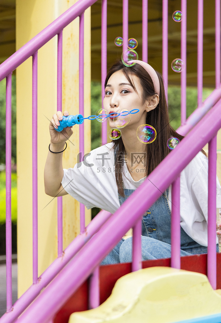 在游乐园里玩吹泡泡的美丽东方女孩高清摄影大图-千库网